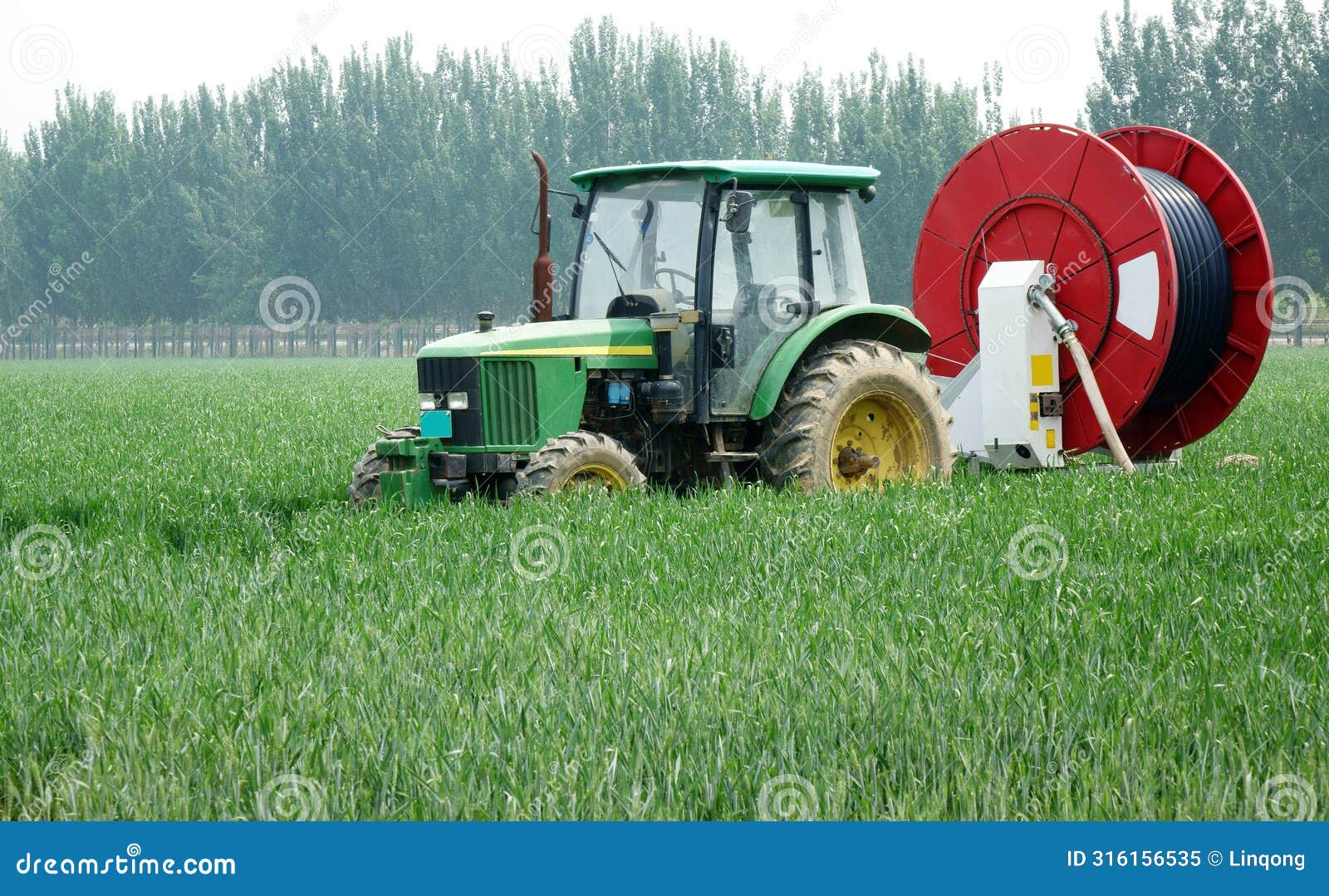 A Tractor Pulling a Reel Irrigation Machine in a Wheat Field. Stock ...
