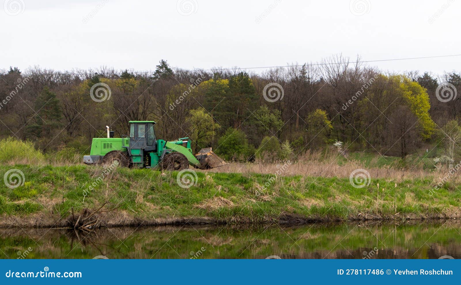 The Tractor Rides Along the Bank of a River or Lake in the Forest ...