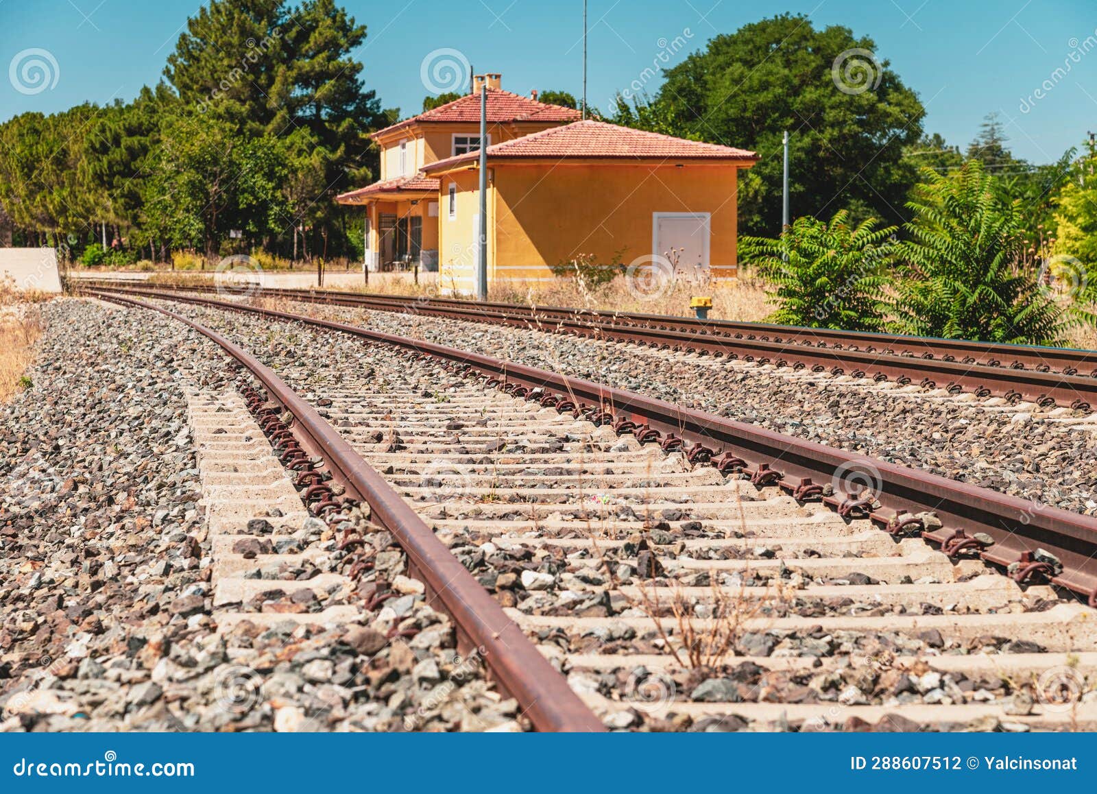 Travel Concept Image with Train Tracks in the Foreground and an Empty Train Station Out of Focus ...