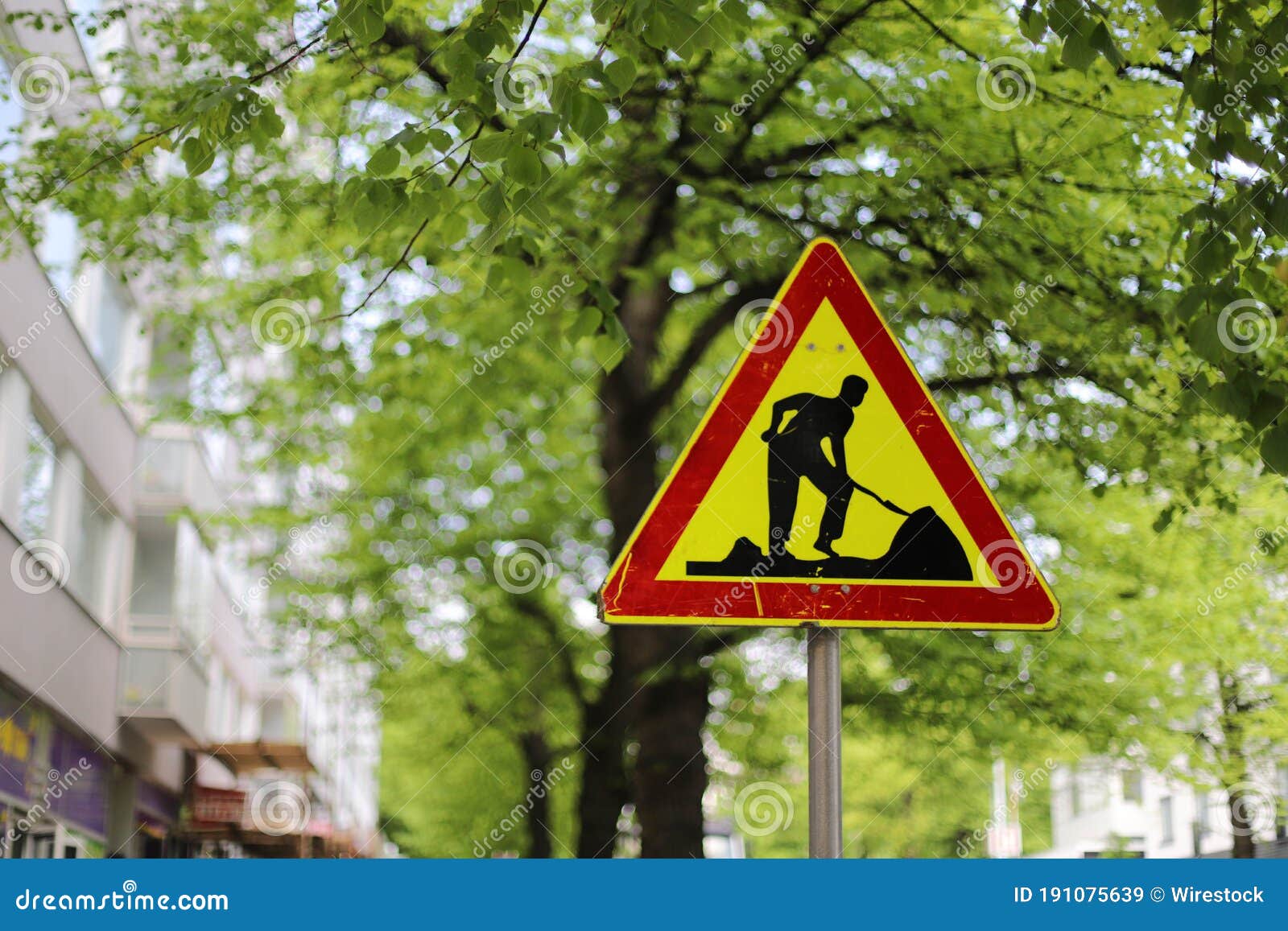 Triangle "Road Construction " Sign on a Post at a Street with Trees ...