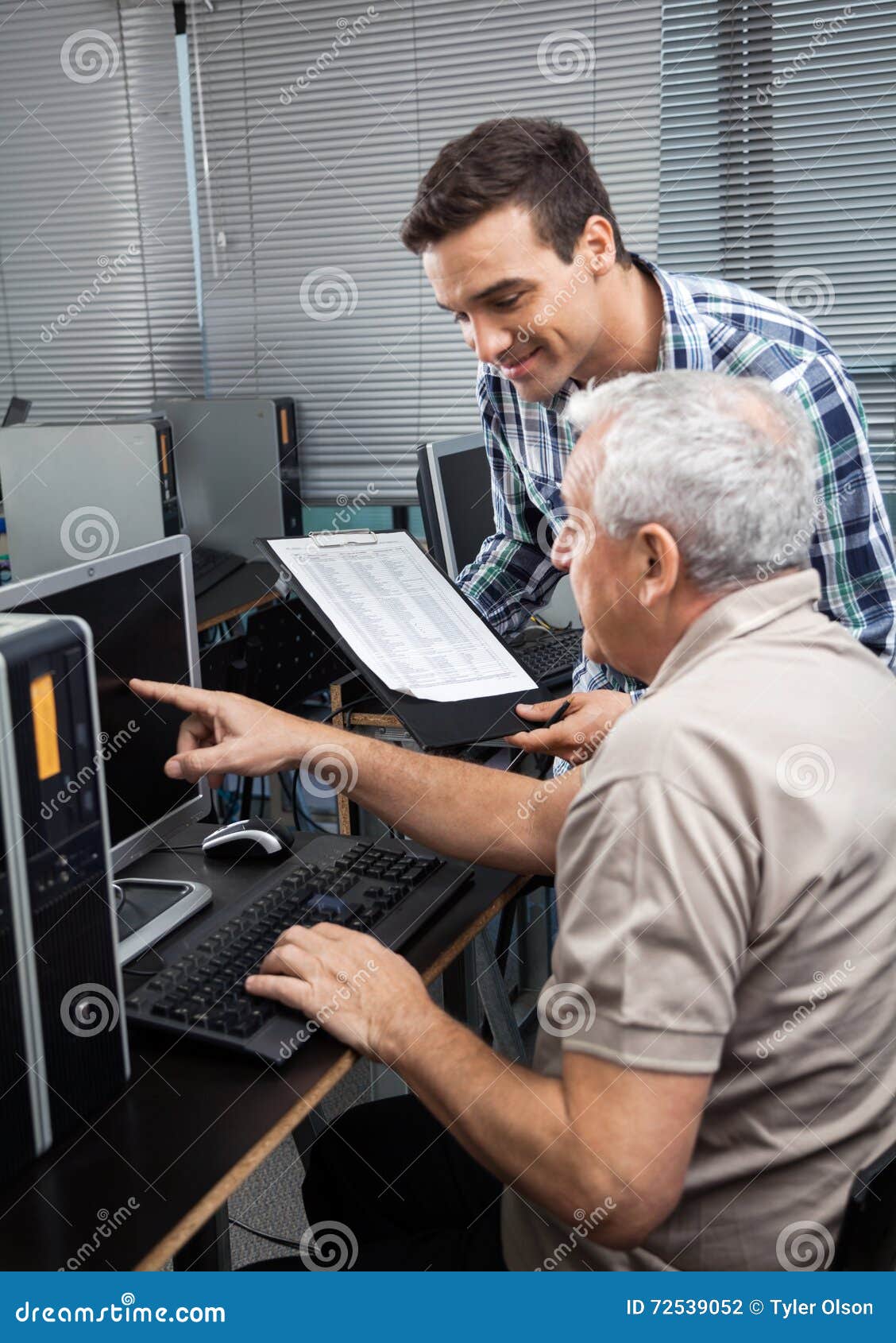 Tutor Holding Clipboard while Assisting Senior Man in Using Comp Stock ...