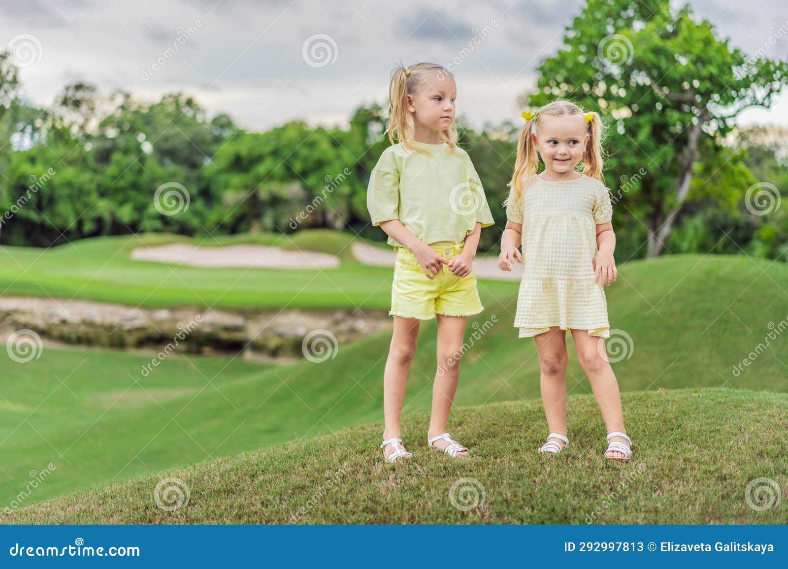 Two Adorable Sisters Share A Heartwarming Moment On A Green Lawn Their
