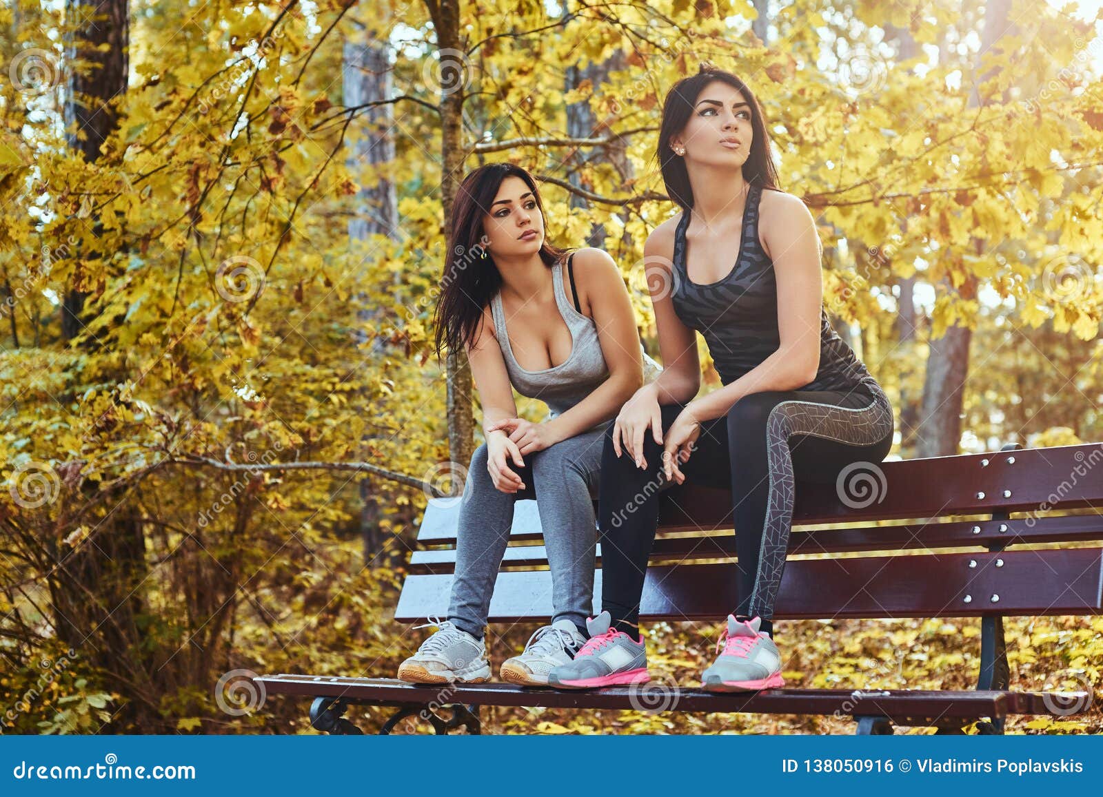 Two Beautiful Girls Wearing Sportswear Sitting On A Bench In The Autumn