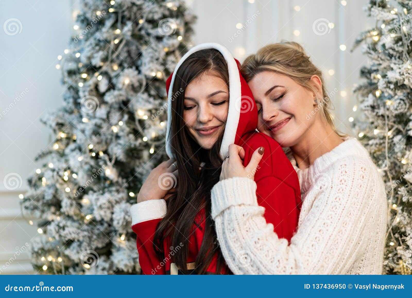 Two Beautiful Sisters In Sweaters Hugging Near The Christmas Tree Stock