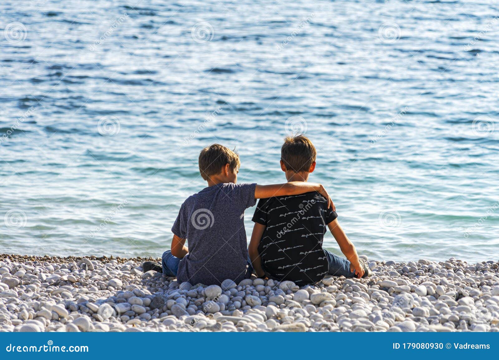 Two Boys Sitting on the Beach, Talking and Throwing Rocks into the Sea ...
