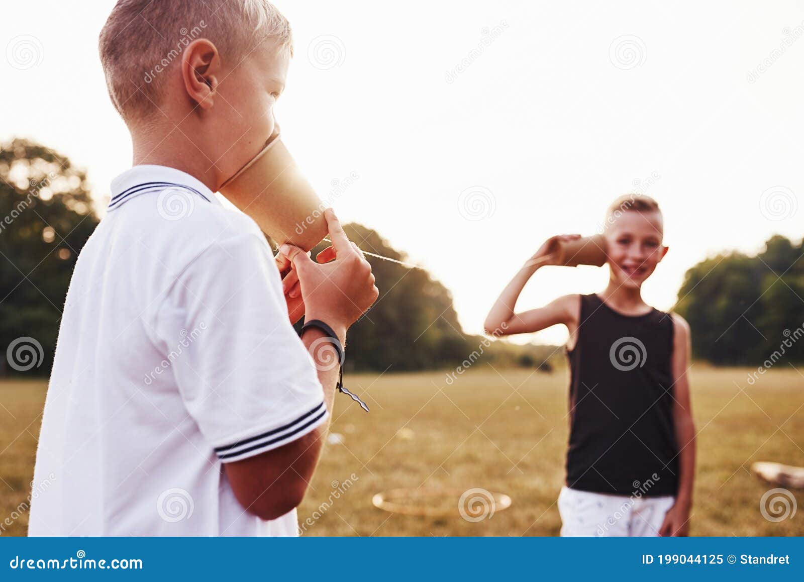 Two Boys Stands in the Field and Talking by Using String Can Phone ...