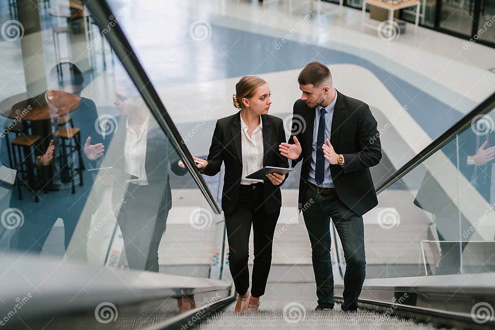 Two Business People Using Tablet Computer while Going Up the Escalator ...
