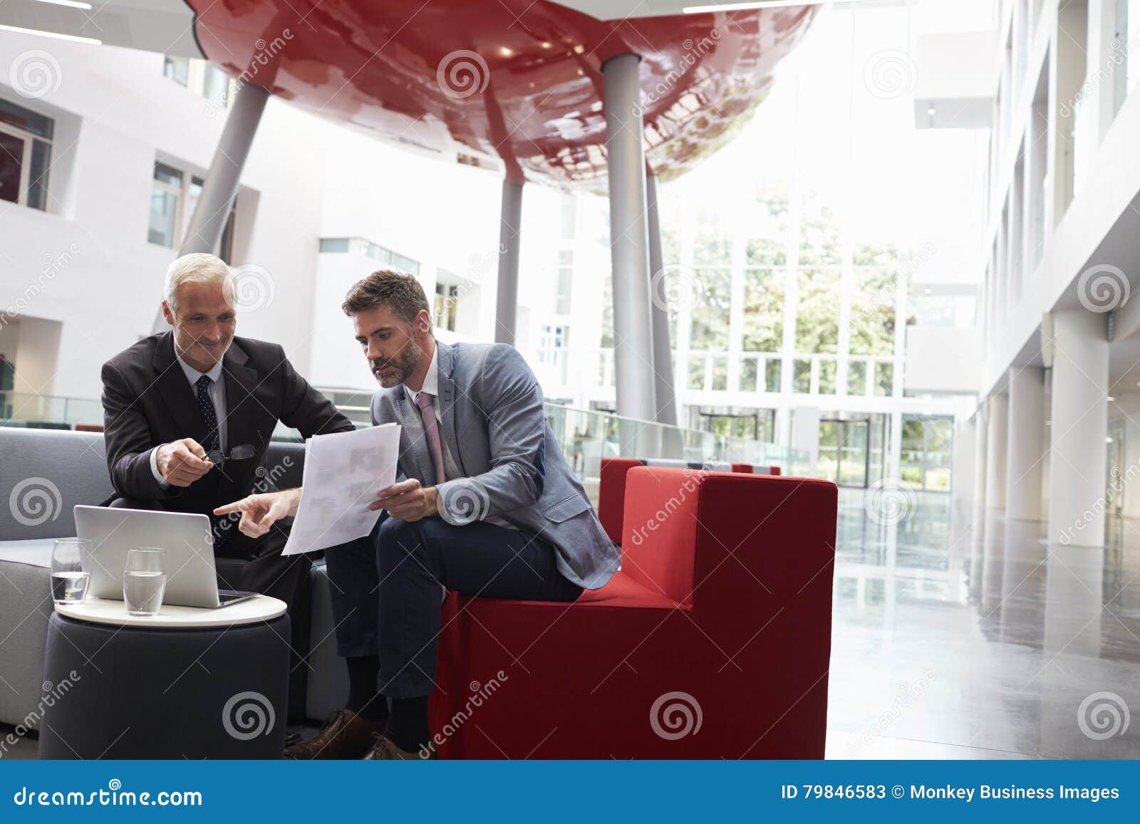 Two Businessmen Discuss Document in Lobby of Modern Office Stock Image ...