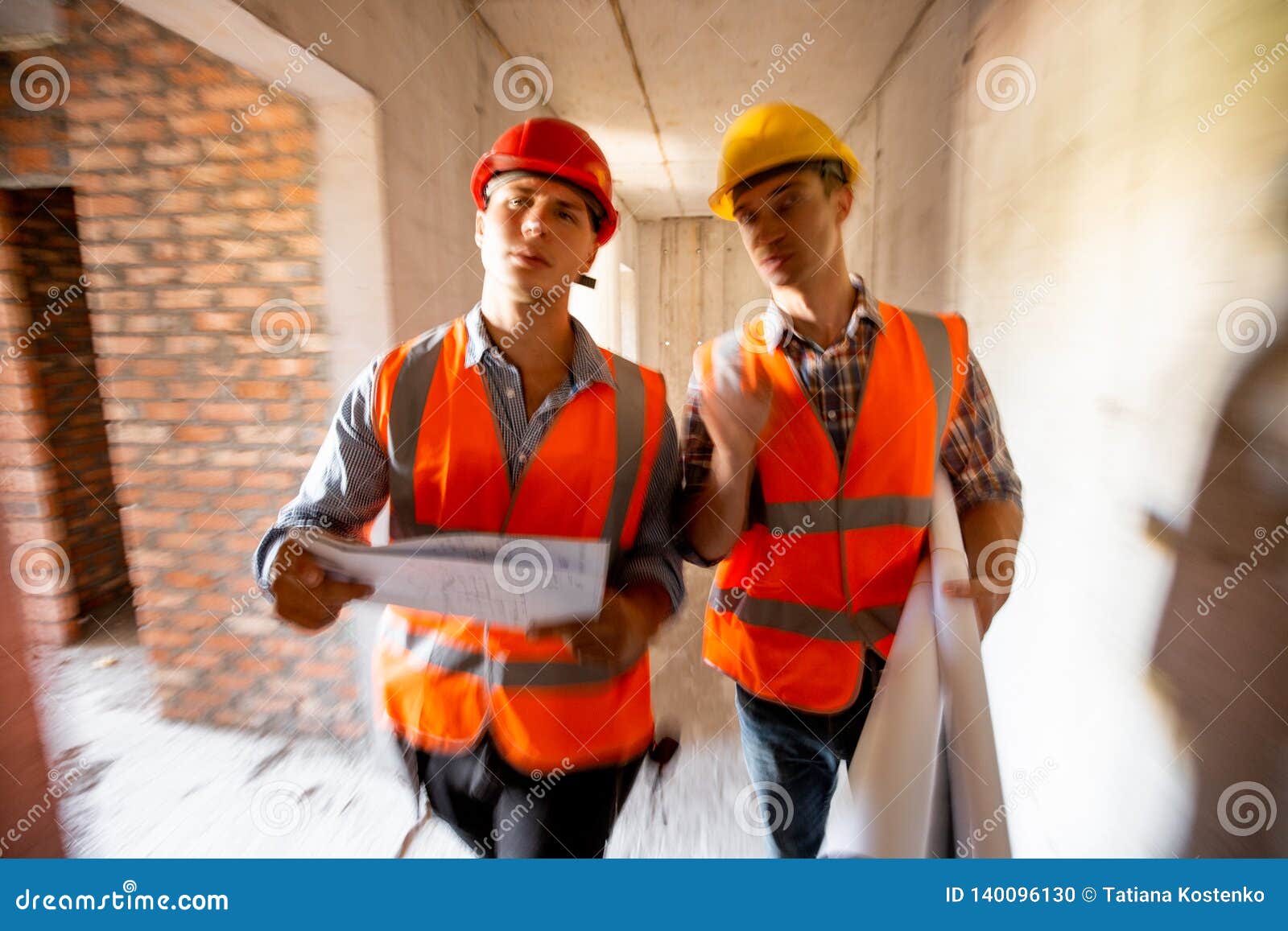 Two Civil Engineers Dressed in Orange Work Vests and Helmets Walk ...