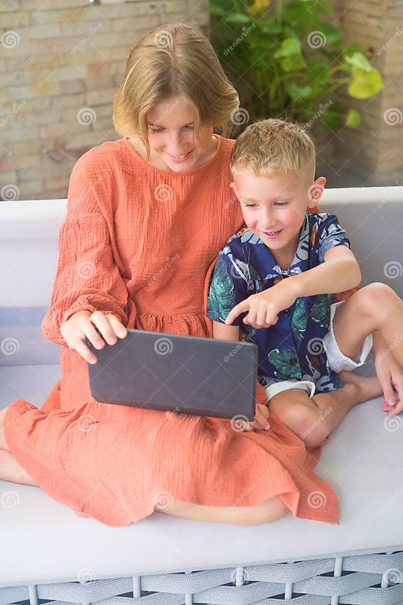 Two Cute Siblings Brother And Sister Sitting On Sofa At Home And Playing On Wireless Tablet
