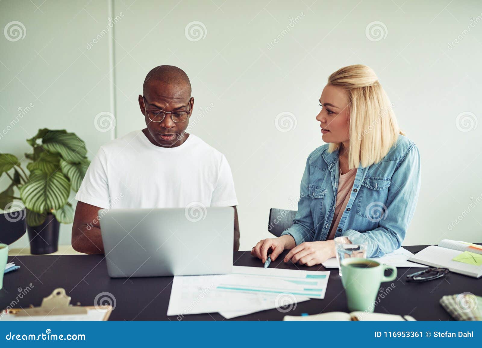 Two Diverse Coworkers Talking Together While Working On A Laptop Stock
