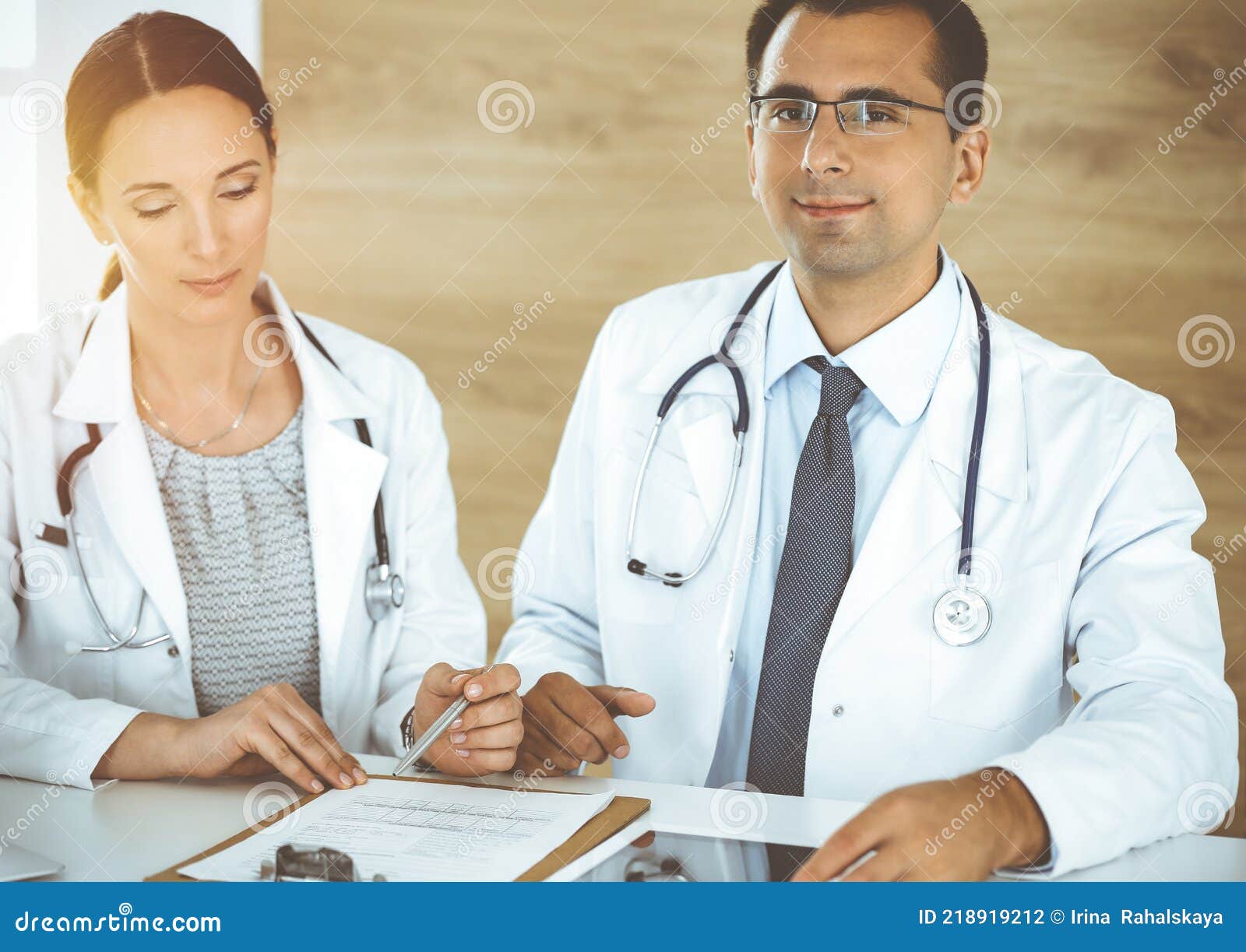 Two Doctors Discussing Treatment Problems while Sitting at the Desk in ...