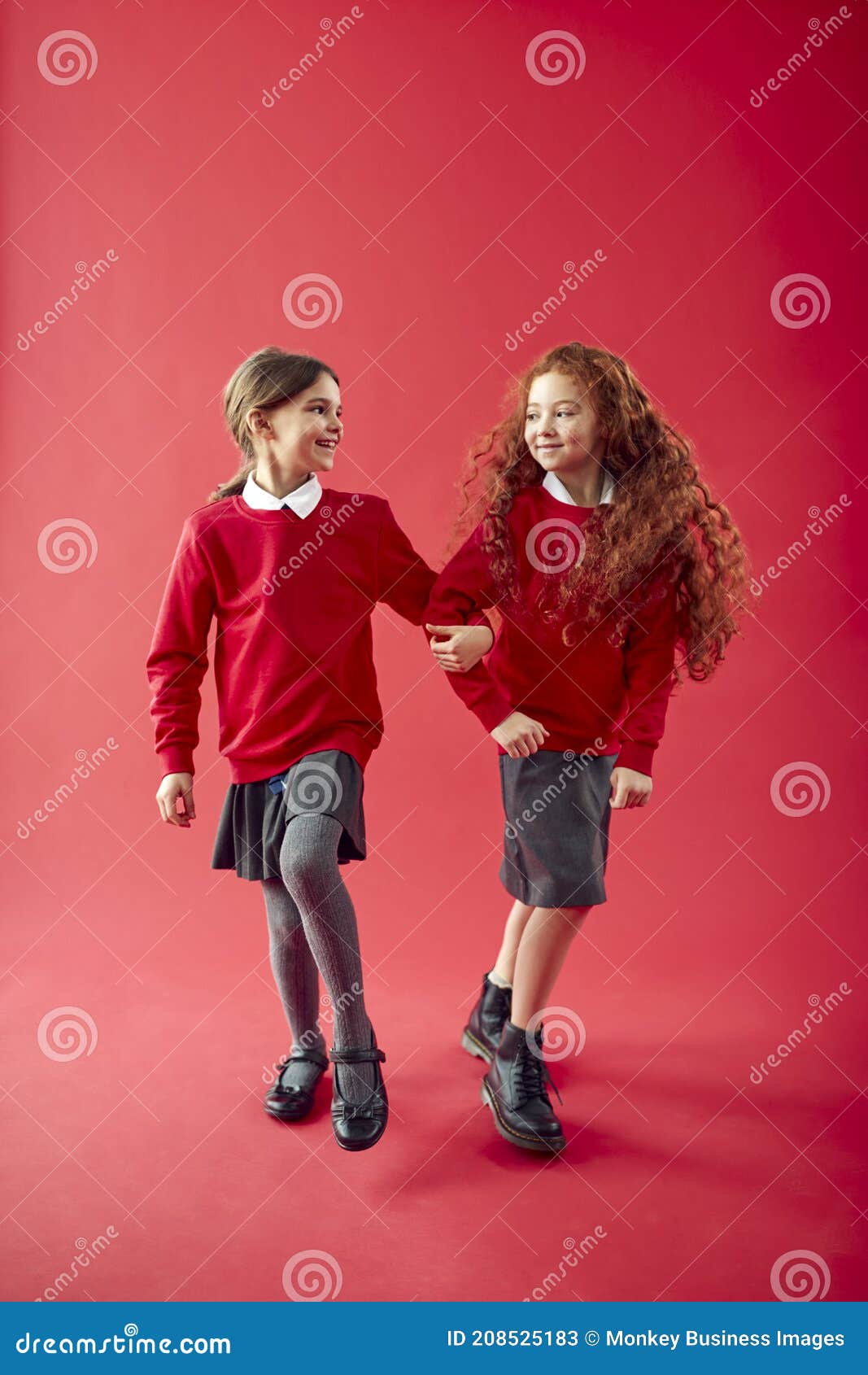 Two Elementary School Pupils Wearing Uniform Linking Arms Against Red ...