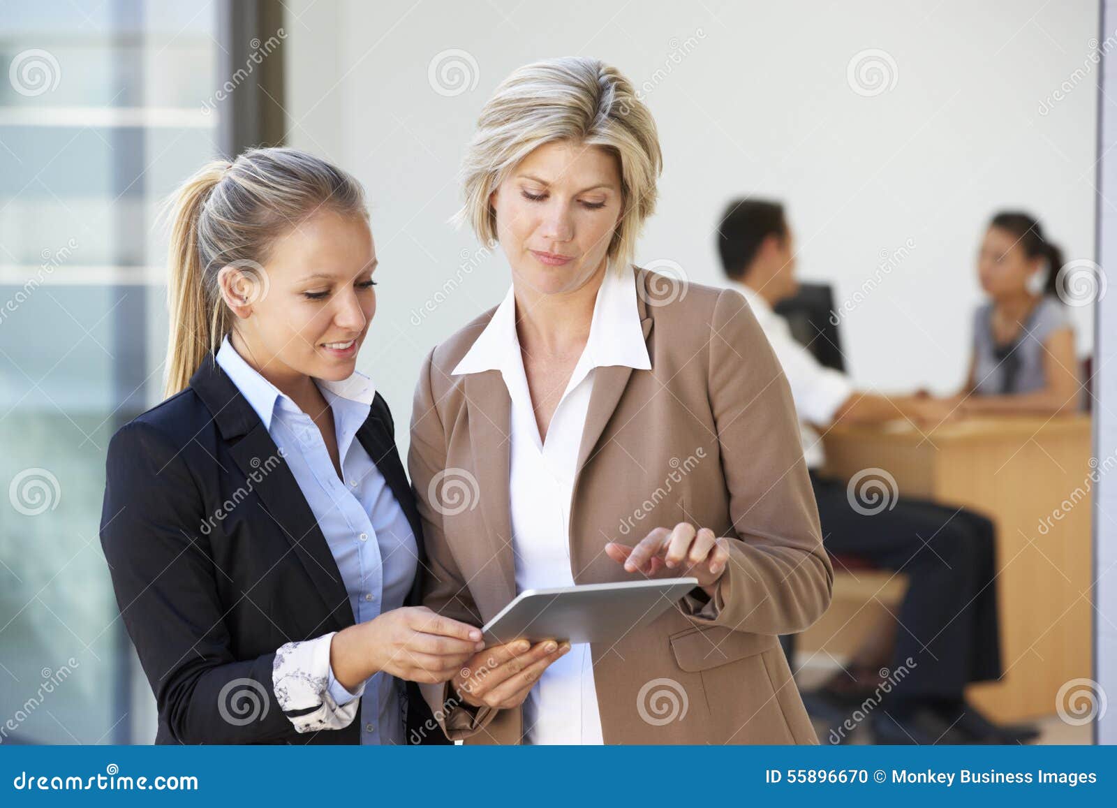 Two Female Executives Looking at Tablet Computer with Office Meeting in ...