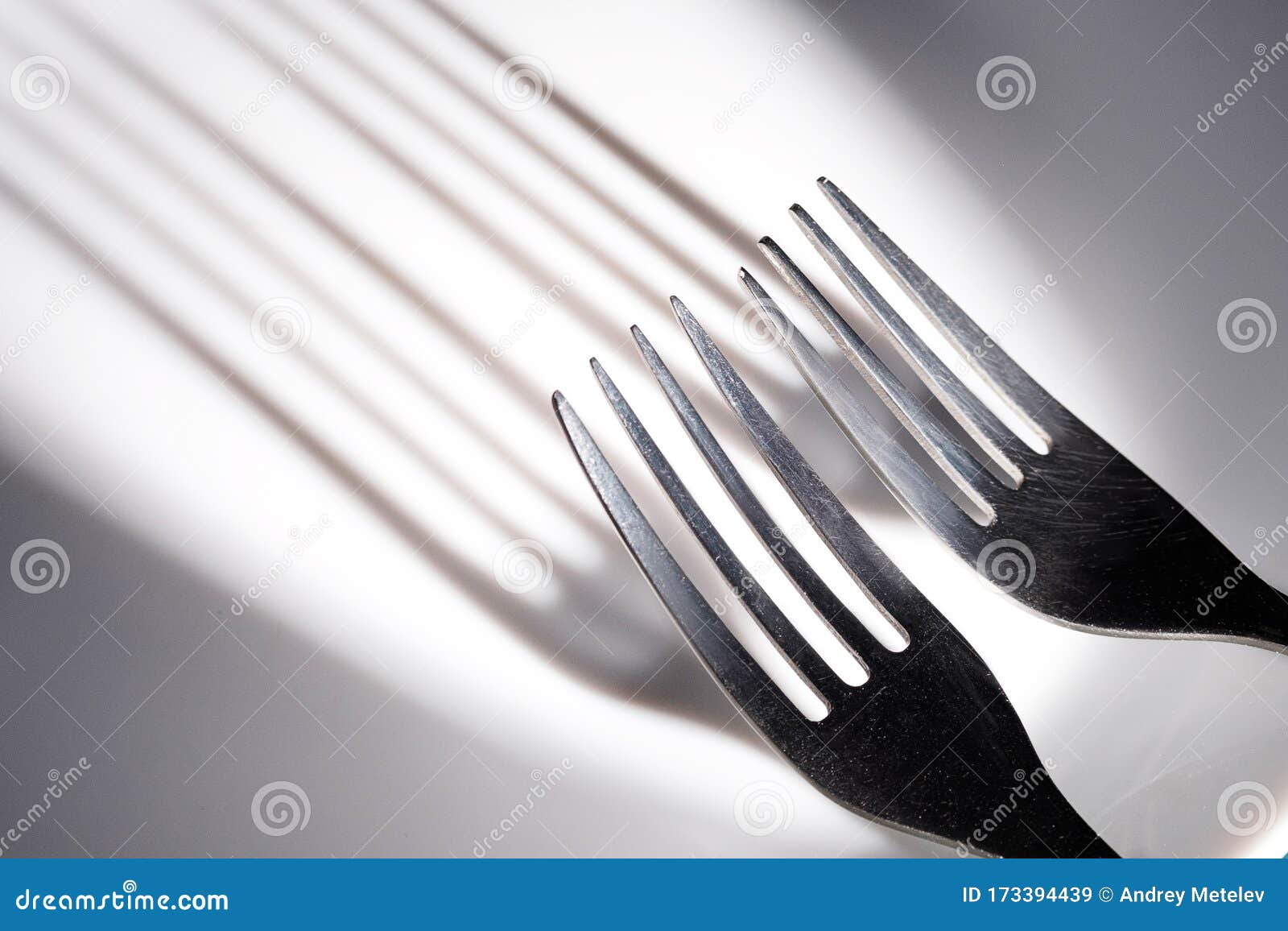 Two Forks Cast a Shadow from Their Teeth Onto a White Ceramic Surface ...