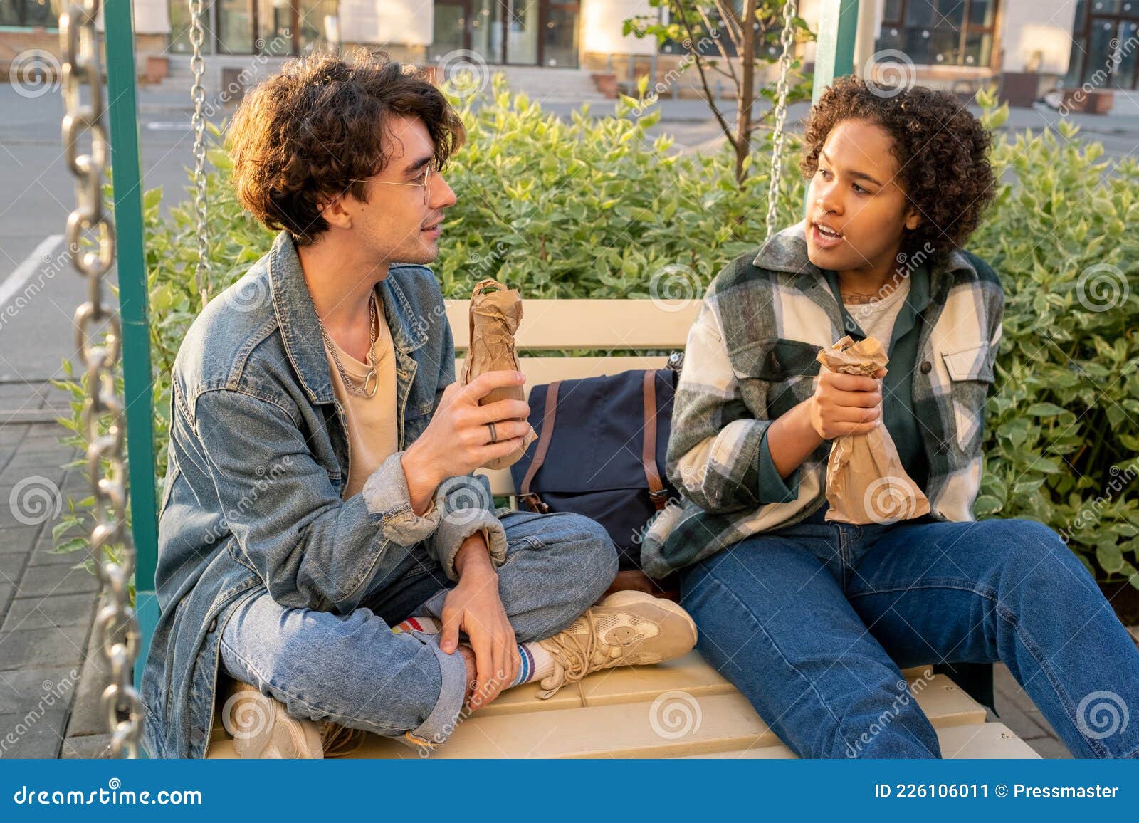 Two Friendly Teenagers with Drinks Talking while Relaxing on Swings ...