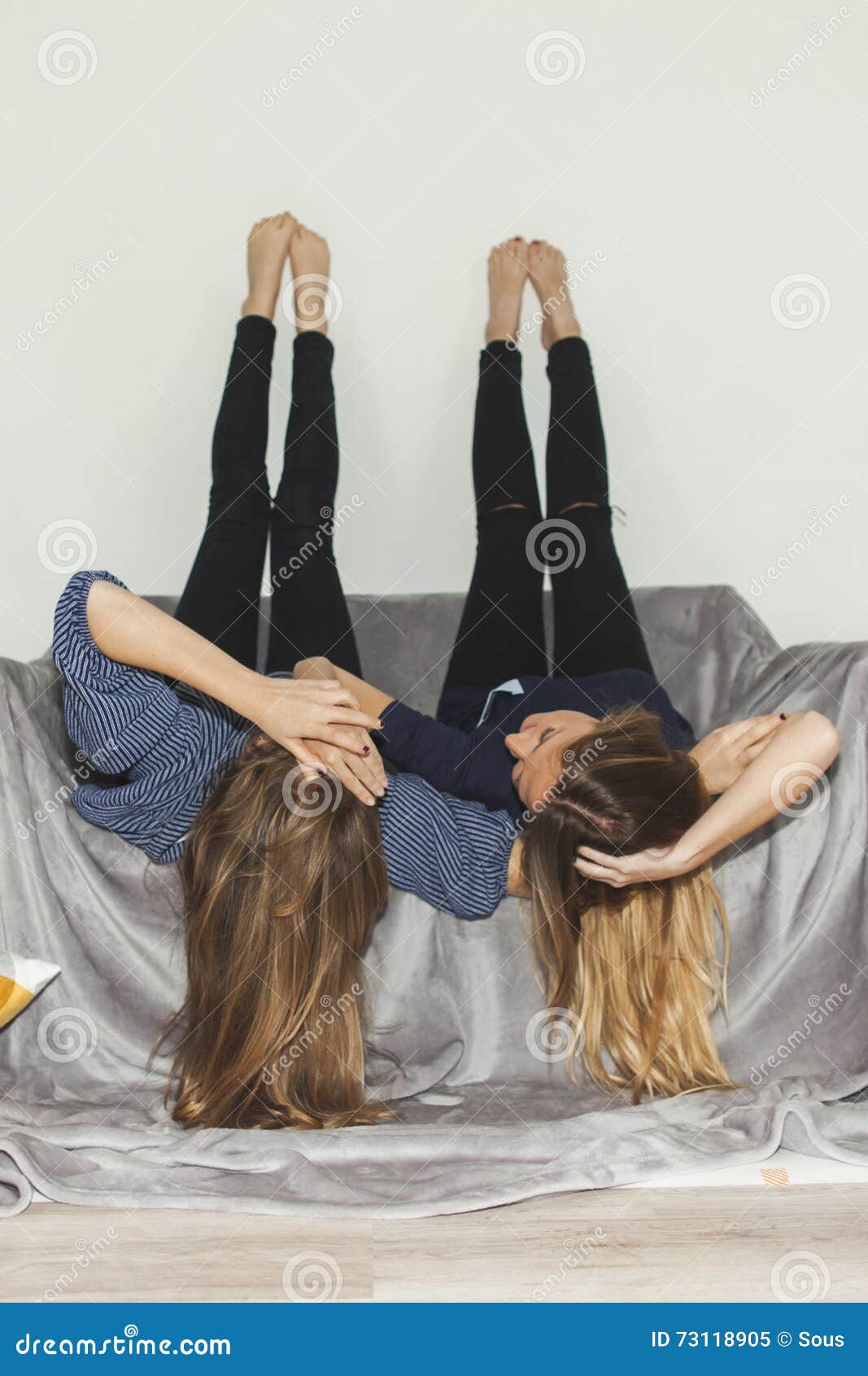 Two Girls Laying Upside Down On A Grey Sofa With Legs Up Stock Image 73118905