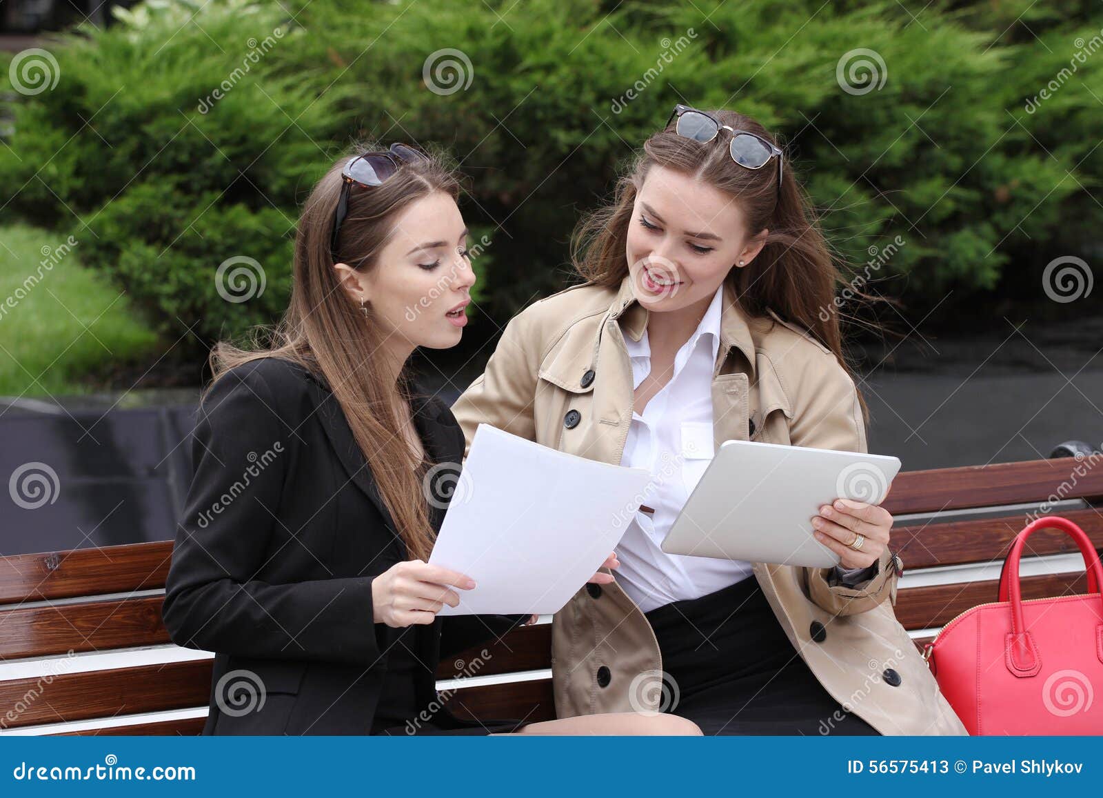 Two Girls with Papers and Tablet Computers Talk on a Park Bench Stock ...