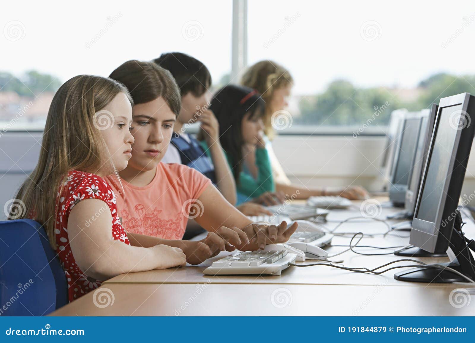 Two Girls (10-12) Using Computer in Computer Lab Children in Background ...