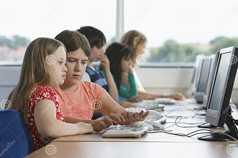 Two Girls (10-12) Using Computer in Computer Lab Children in Background ...