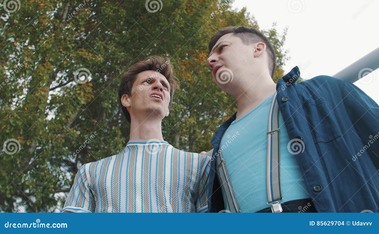 Two Guys Stand Under Trees Looking Down, Talking and Start Shouting ...