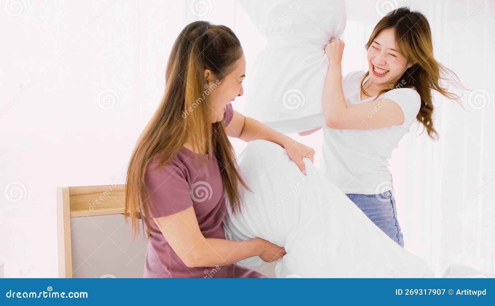 Two Happy And Attractive Asian Women Having A Pillow Fight With Smiles