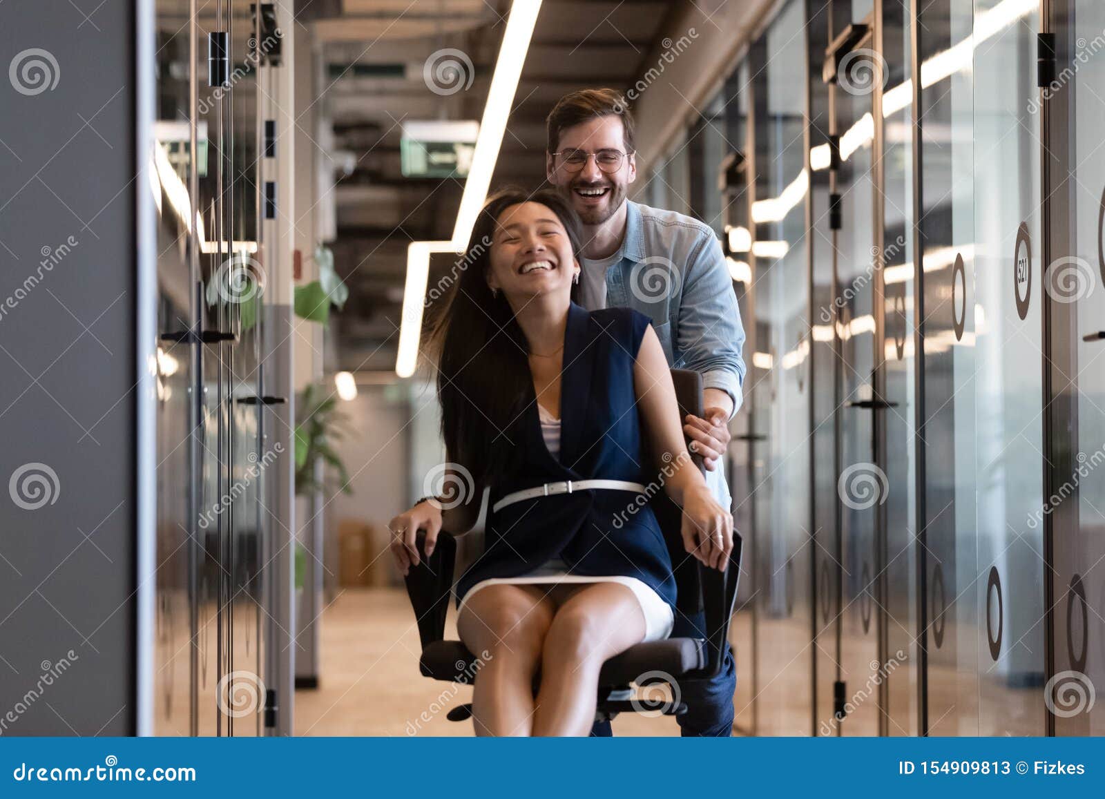 Two Happy Coworkers Having Fun Ride On Chair In Office Stock Image
