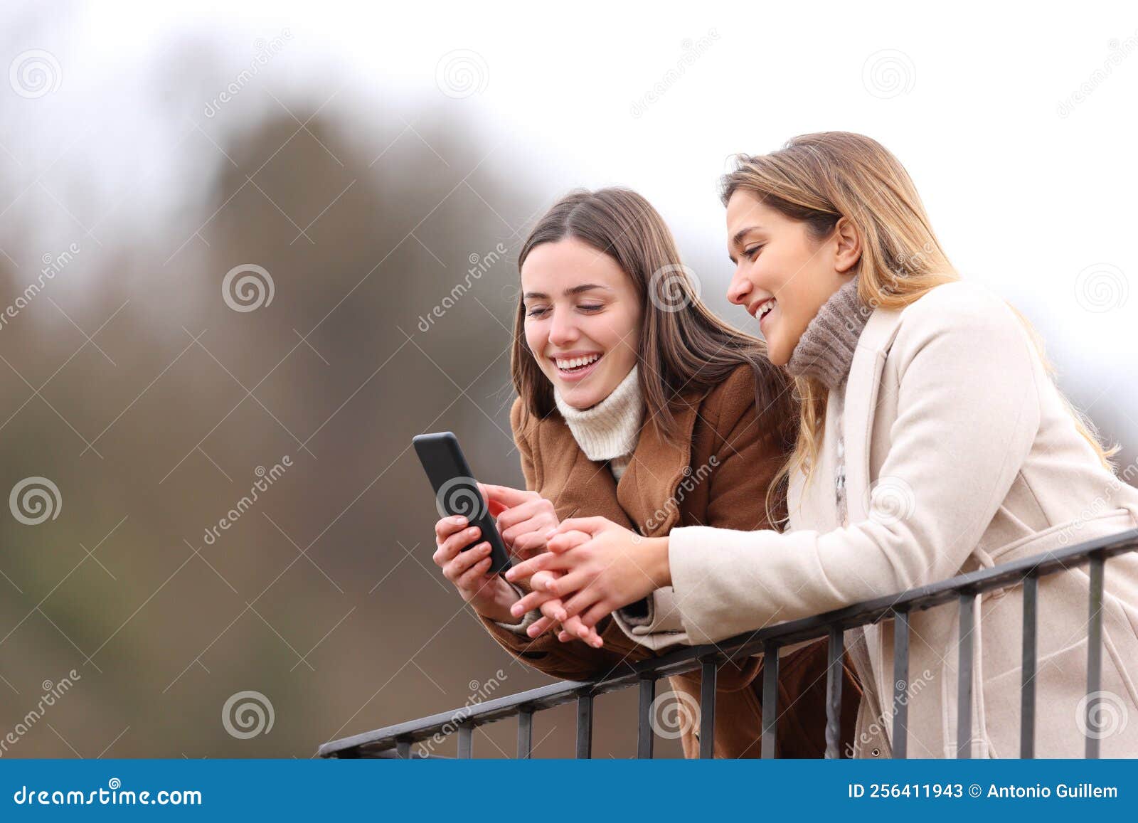 Two Happy Friends Checking Phone in Winter in a Balcony Stock Image ...