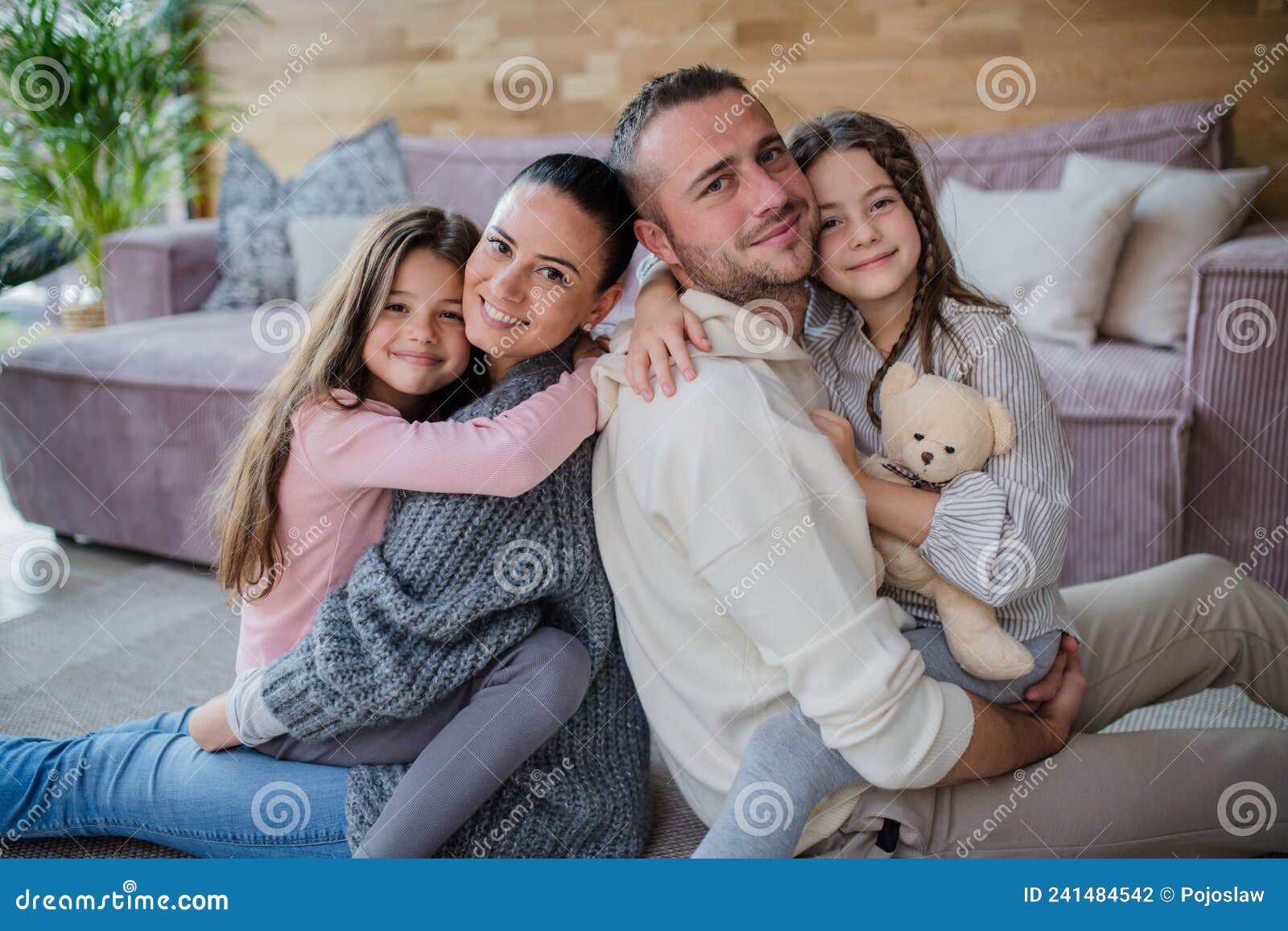 Two Happy Sisters With Mother And Father Sitting On Floor Hugging And