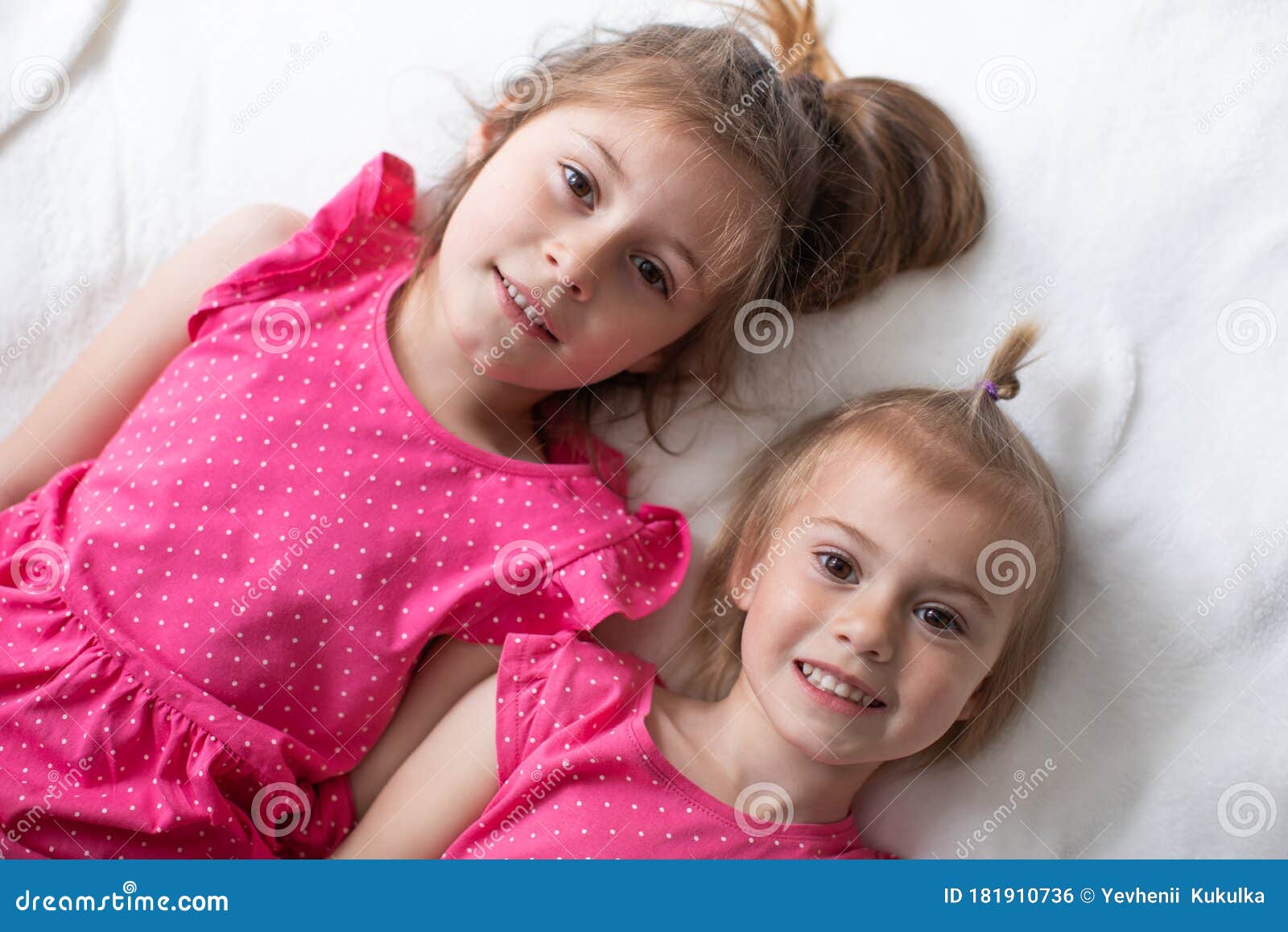 Two Happy Sisters in Pink Dresses are Lying on the Bed and Smiling ... Two Happy Sisters in Pink Dresses are Lying on the Bed and Smiling ...