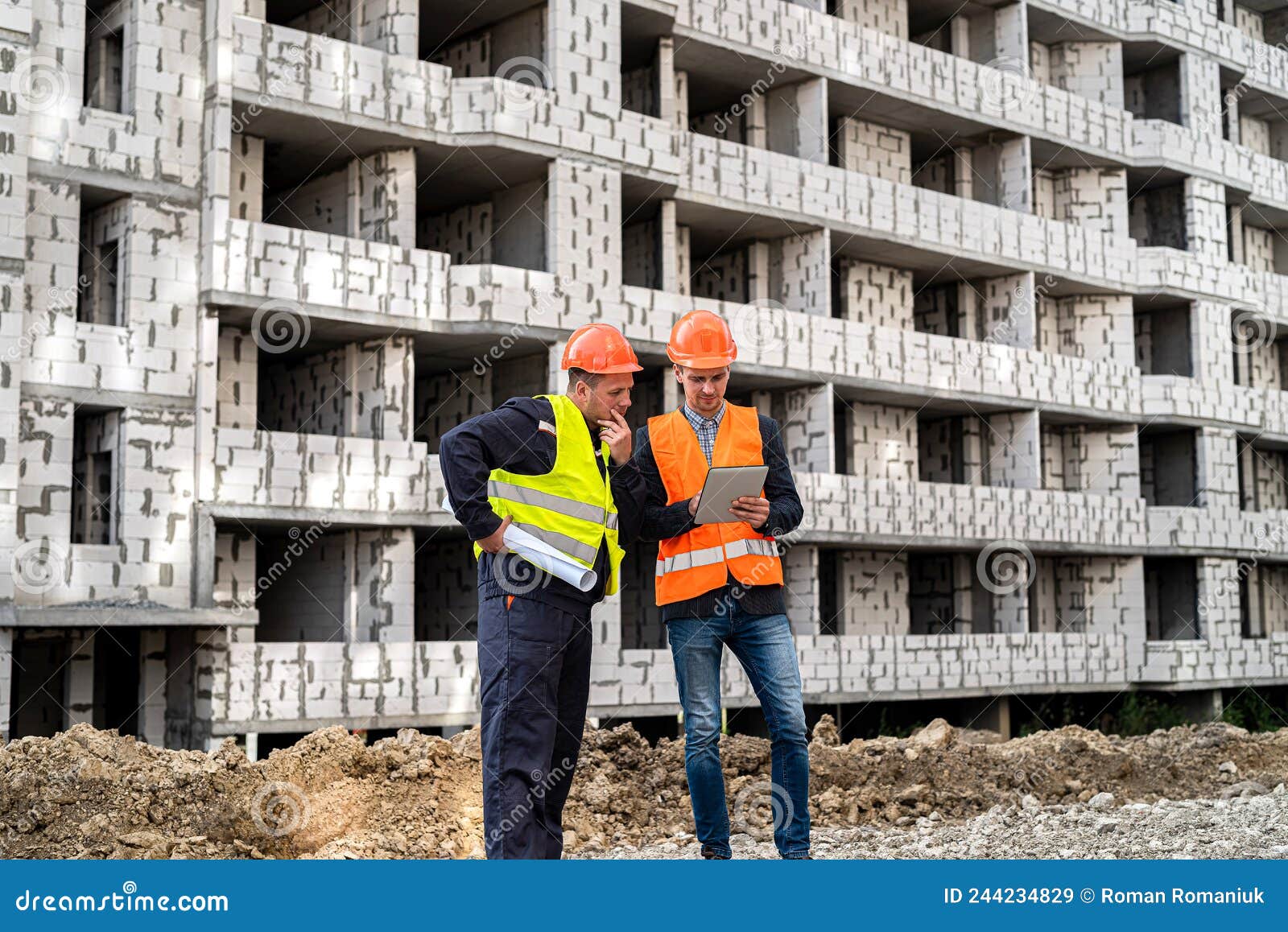 Two Important Workers in Overalls and Helmets Look at the Tablet in the ...