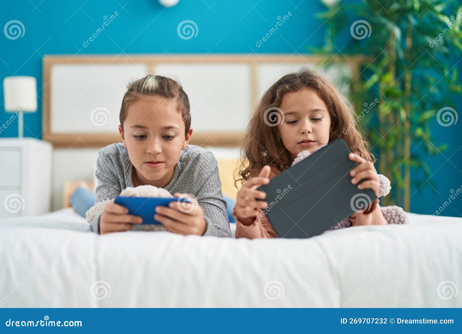 Two Kids Using Smartphone and Touchpad Lying on Bed at Bedroom Stock ...