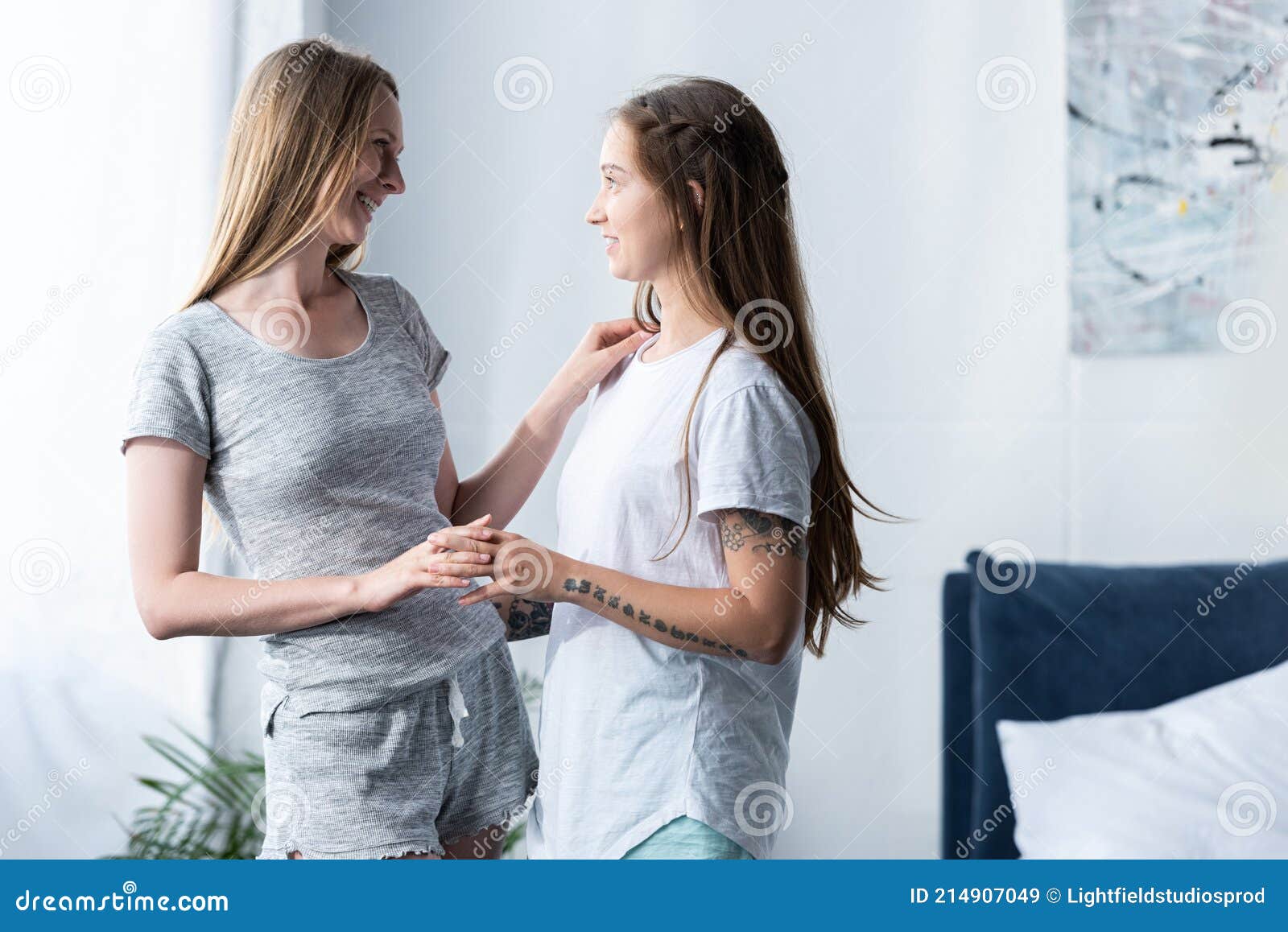 Two Lesbians Holding Hands And Looking At Each Other In Bedroom Stock