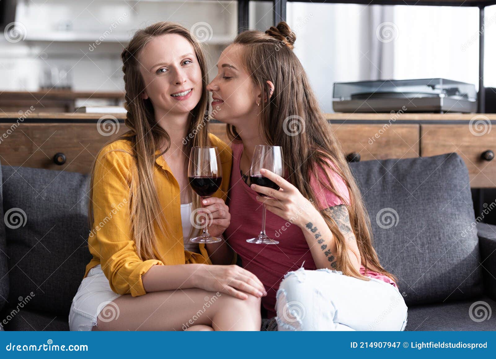 Two Lesbians Holding Wine Glasses While Sitting On Sofa In Living Room