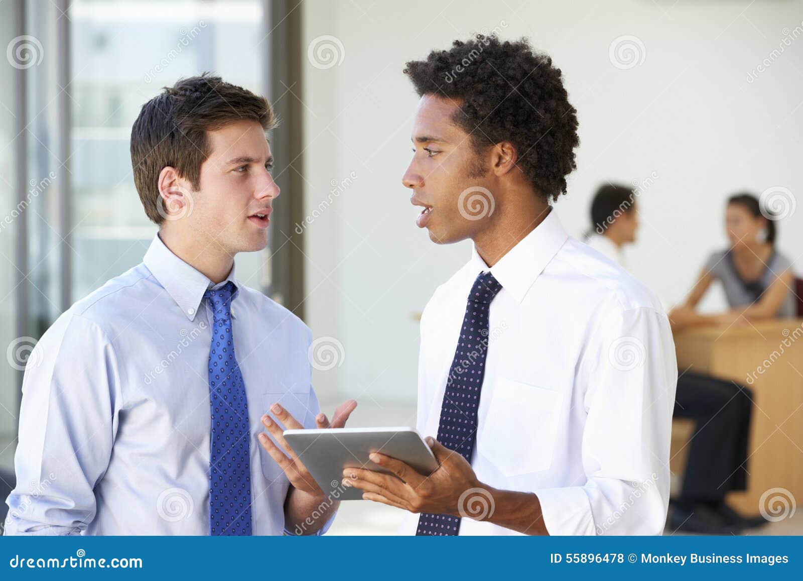 Two Male Executives Looking at Tablet Computer with Office Meeting in ...