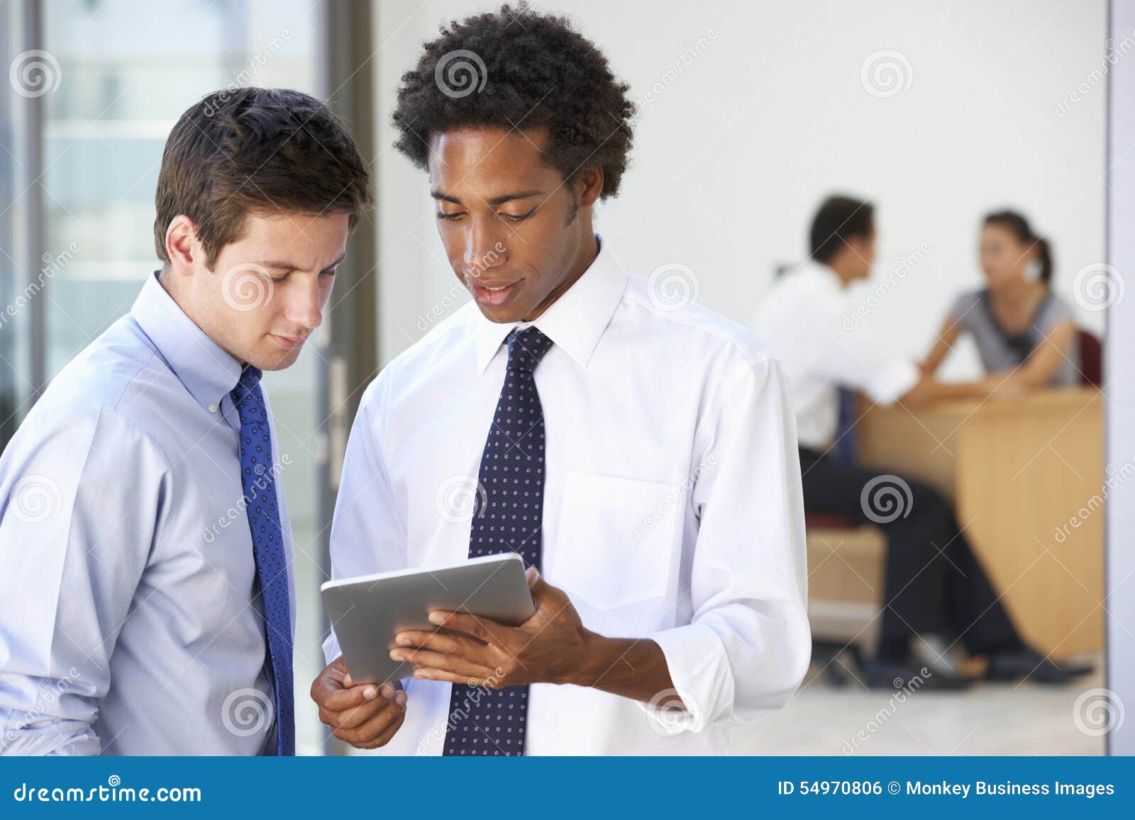 Two Male Executives Looking at Tablet Computer with Office Meeting in ...