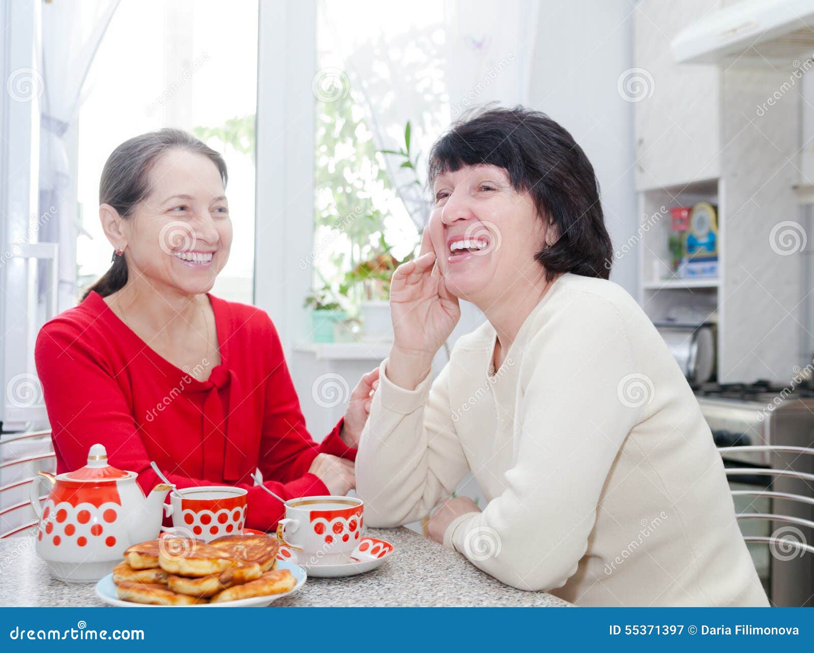 Two Mature Women Laughing at Kitchen Table Stock Image - Image of ...