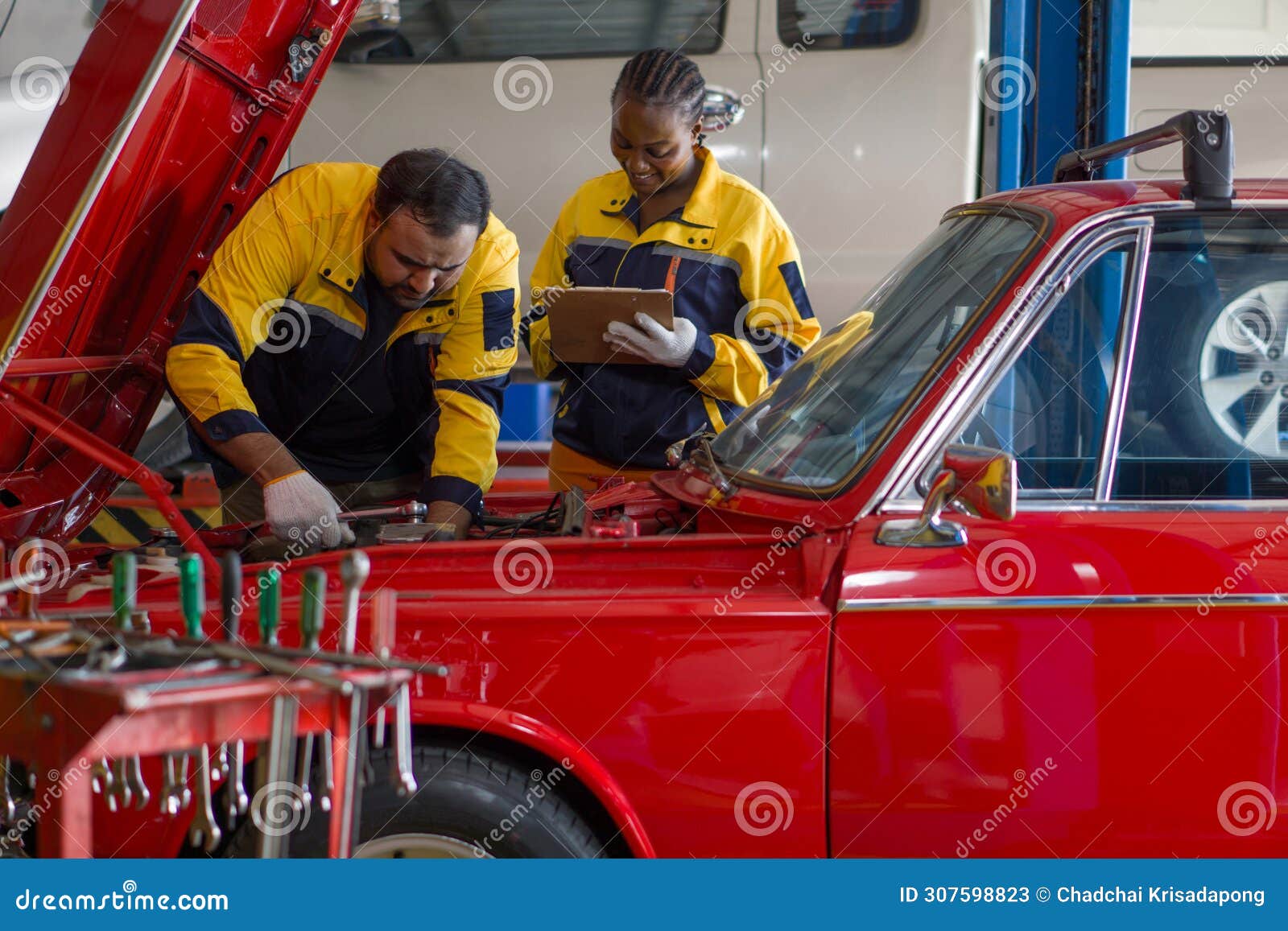 Two Mechanics Dressed in Uniform Fix a Car Together in a Garage Full of ...