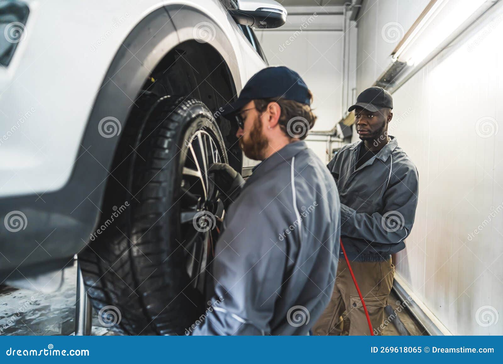 Two Mechanics at Work. One Changing a Tyre, Another Looking at Thr ...