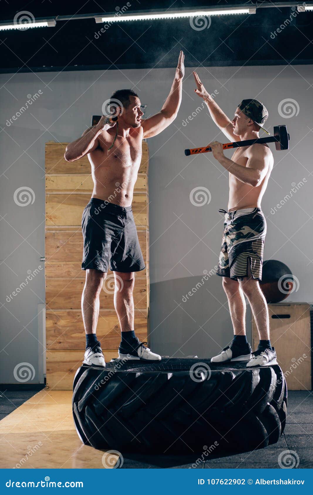 Two Men Doing High Five while Standing on Tire and Holding ...