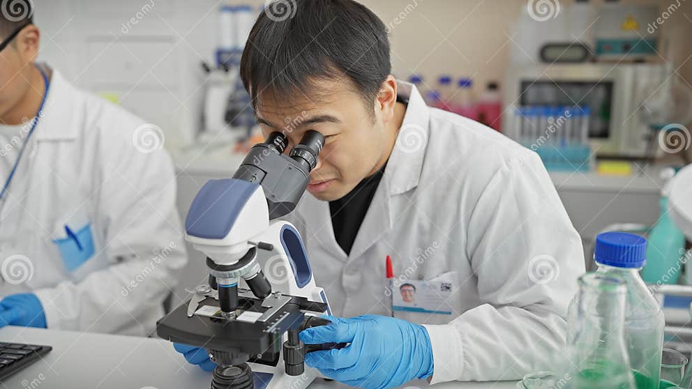Two Men in Lab Coats Examine Samples with a Microscope in a Scientific ...