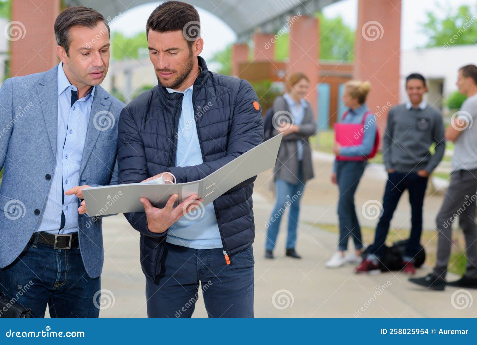 Two Men Looking at Folder while Students Wait in Background Stock Photo ...