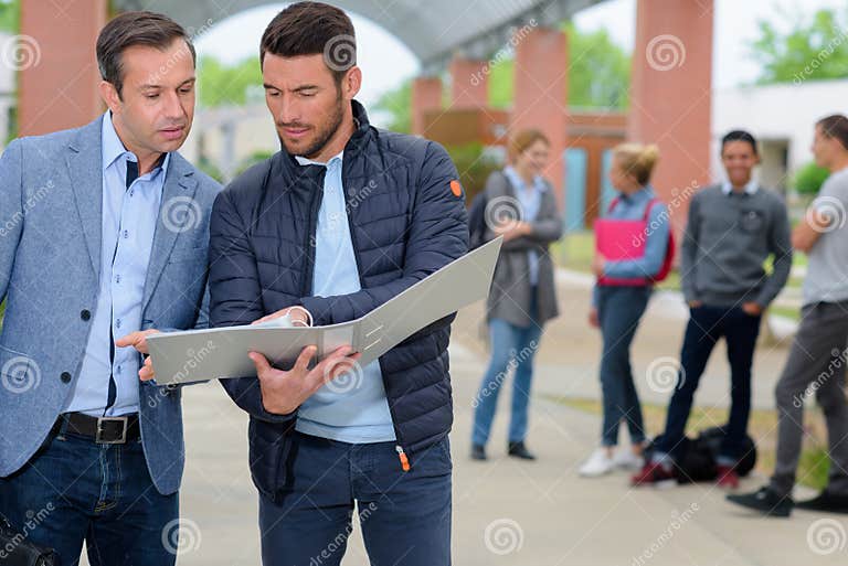 Two Men Looking at Folder while Students Wait in Background Stock Photo ...