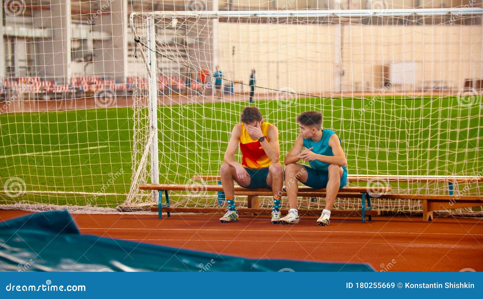 Two Men Sitting on the Bench while the Pole Vault Training on the ...