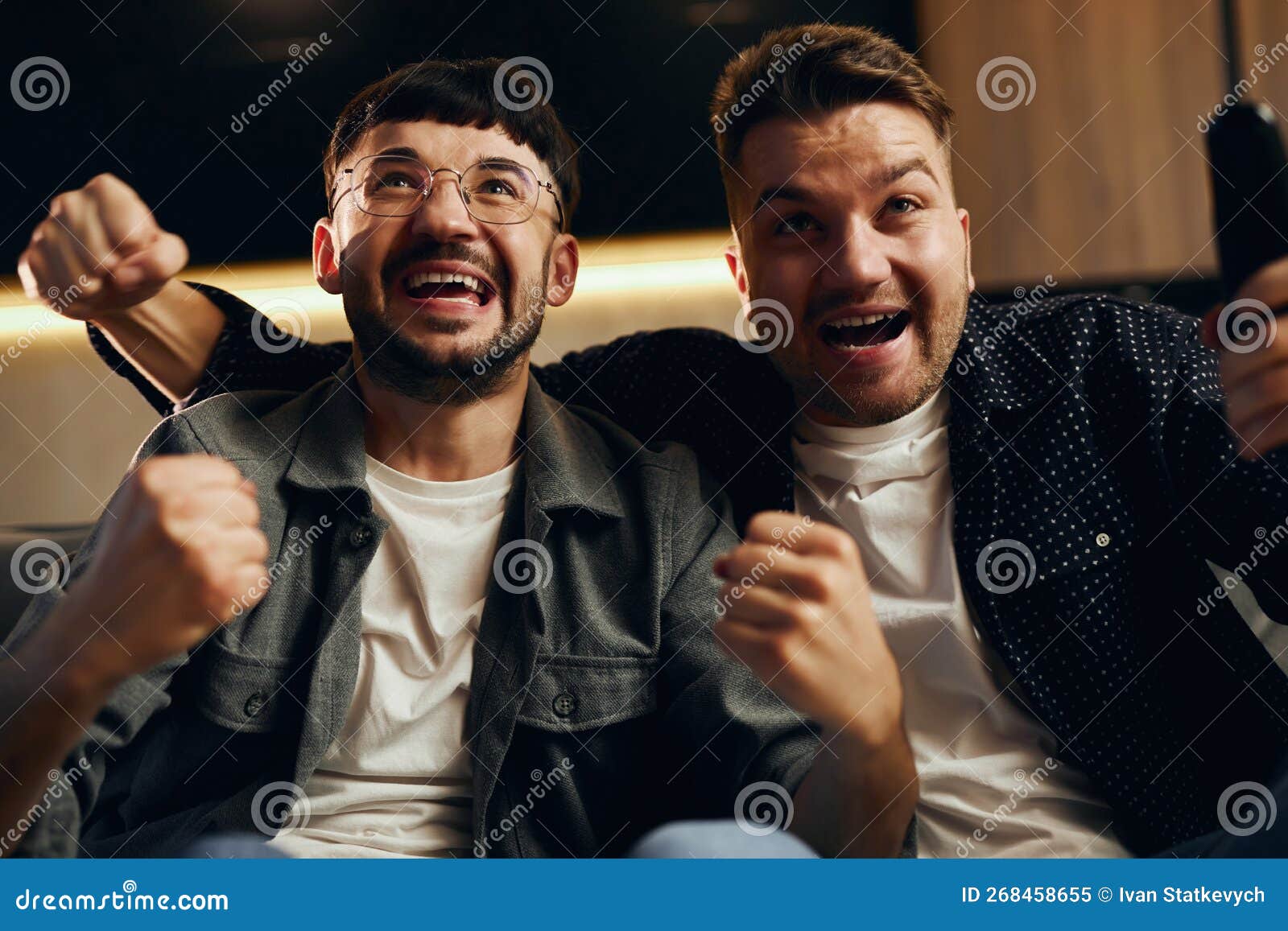 Two Men are Sitting on the Sofa at Home and Cheering for Their Football ... Two Men are Sitting on the Sofa at Home and Cheering for Their Football ...