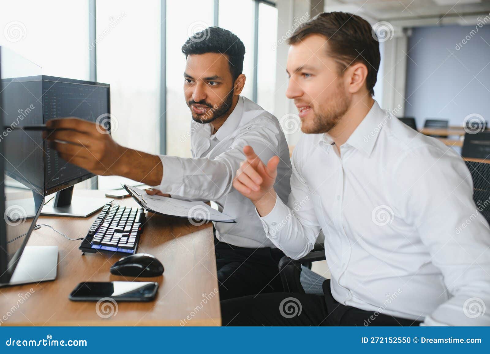 Two Men Traders Sitting at Desk at Office Together Looking at Data ...