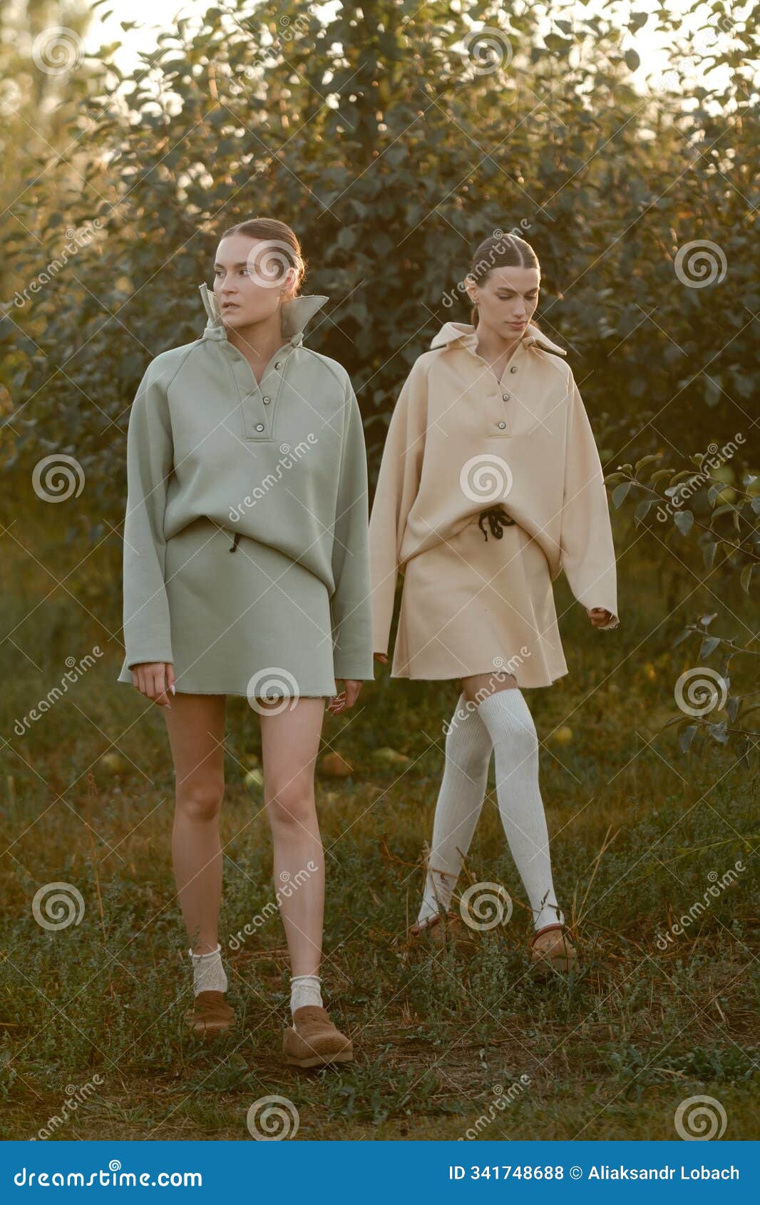 Two Models in Stylish Tracksuits Pose in Apple Orchard at Sunset . the ...