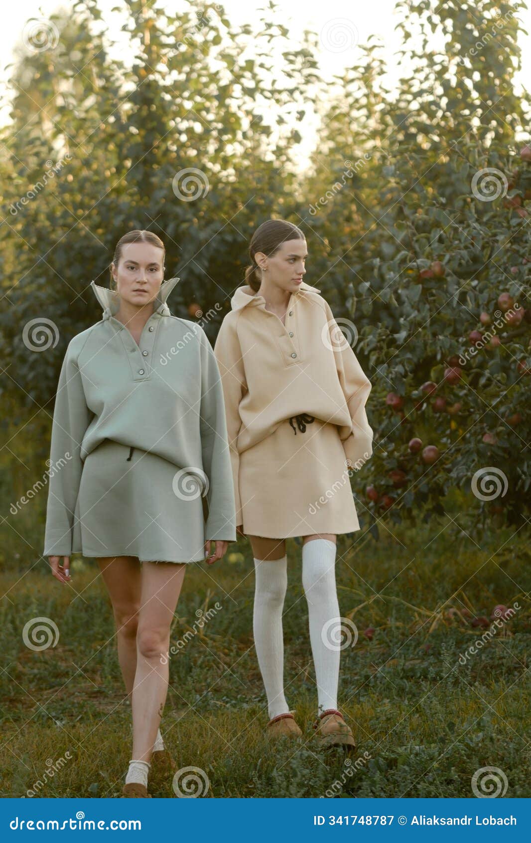 Two Models in Stylish Tracksuits Pose in Apple Orchard at Sunset . the ...
