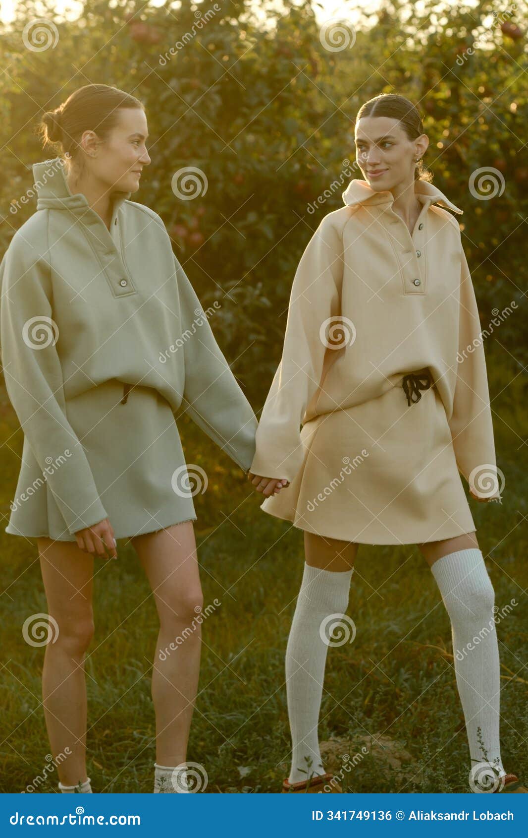 Two Models in Stylish Tracksuits Pose in Apple Orchard at Sunset . the ...