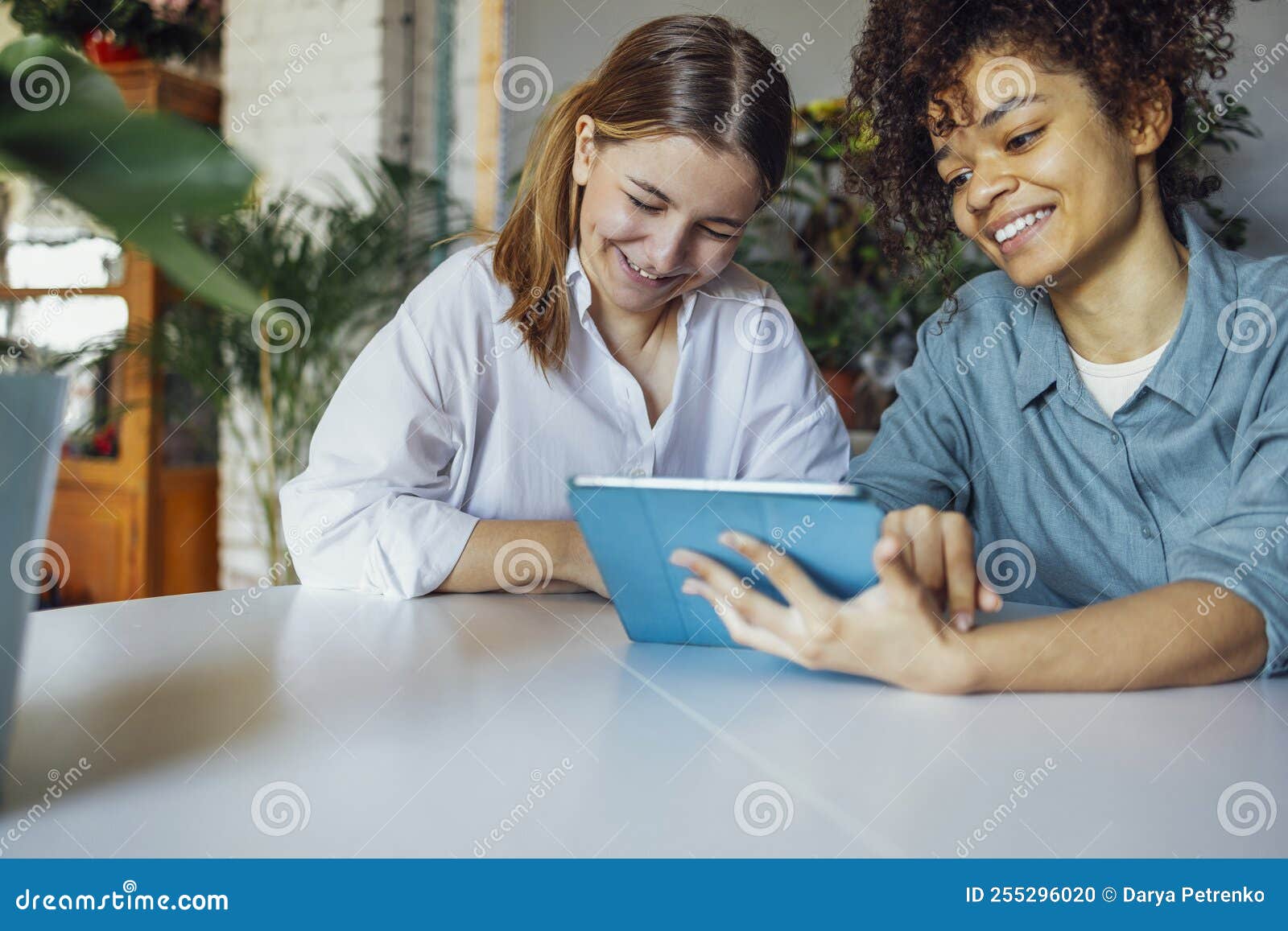 Two Multiethnic Female Students Sitting at Table with Tablet Pc ...